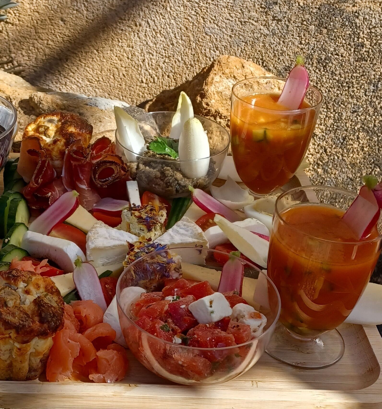 Diversos alimentos, incluindo queijo, embutidos e um copo de chá gelado, dispostos sobre uma tábua de madeira.
