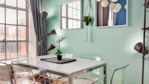 Uma sala de jantar moderna com mesa branca, cadeiras transparentes e uma planta pendente.