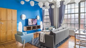 Uma sala de estar moderna com uma parede azul de destaque, armários de madeira, um sofá cinza e uma área de jantar com mesa de vidro.