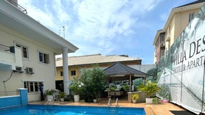 Piscina com deck revestido, rodeada por edifícios e plantas em vasos.