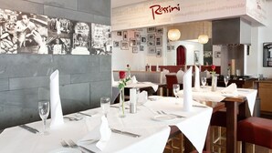 Interior de restaurante com mesas preparadas para refeições, parede com fotografias emolduradas e uma placa sobre as mesas.