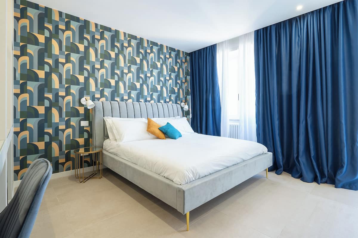 Quarto moderno com parede estampada, cama com roupa de cama branca e cortinas azuis.