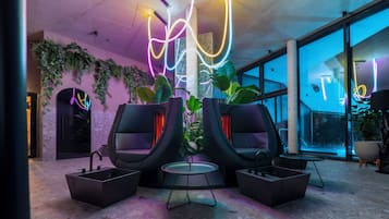 Uma área de estar moderna com assentos pretos, uma mesa central e luzes neon.