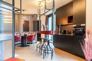 Uma cozinha moderna com forno embutido e uma sala de jantar com cadeiras vermelhas e mesa redonda.
