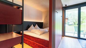 Quarto moderno com cama vermelha, escrivaninha de madeira e porta de vidro deslizante para uma varanda.