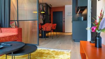 Uma sala de estar moderna com um sofá vermelho, uma mesa de centro preta e um tapete amarelo. Há uma área de jantar com cadeiras vermelhas e uma cozinha com geladeira e fogão.