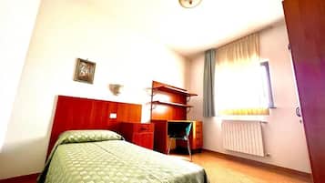 Quarto com cama, escrivaninha, cadeira, radiador e janela com cortinas.