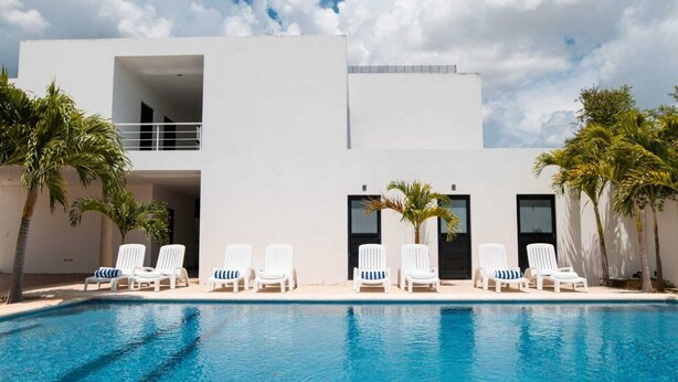 Um edifício moderno com piscina, espreguiçadeiras brancas e palmeiras.