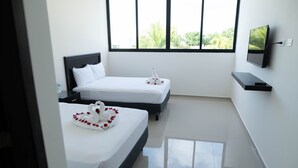 Quarto de hotel com duas camas, TV fixada na parede e janela com vista para o verde.