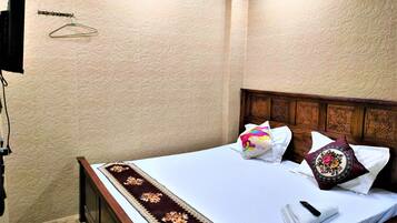Cama bem arrumada com colcha floral, cabeceira de madeira e um cabide suspenso.
