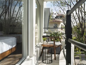 Uma varanda com uma cama, uma mesa pequena com uma cadeira e vista para um edifício com telhado de azulejos.