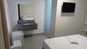 Quarto de hotel com cama, pia com espelho, televisão na parede e uma porta.