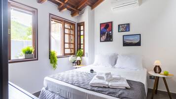 Quarto com cama, duas janelas, ar-condicionado na parede e uma mesinha de cabeceira com abajur e uma maçã.