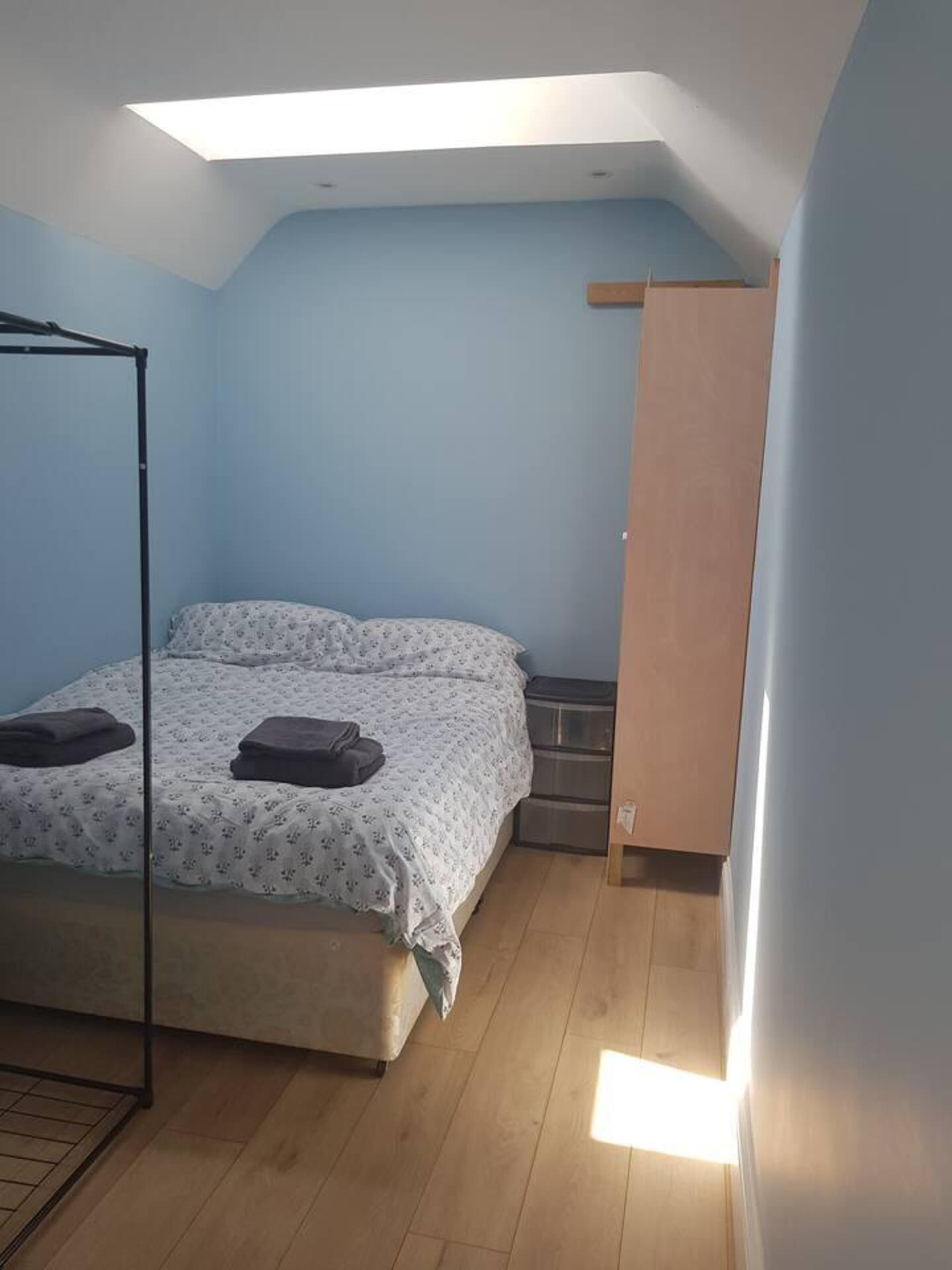 Quarto com cama, guarda-roupa e claraboia.