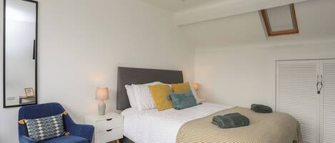 Quarto com cama, cadeira, mesa de cabeceira, espelho e guarda-roupa.