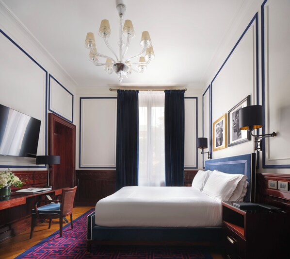 Quarto de hotel com uma cama grande, uma escrivaninha com cadeira, televisão, candelabro e luminária na parede.