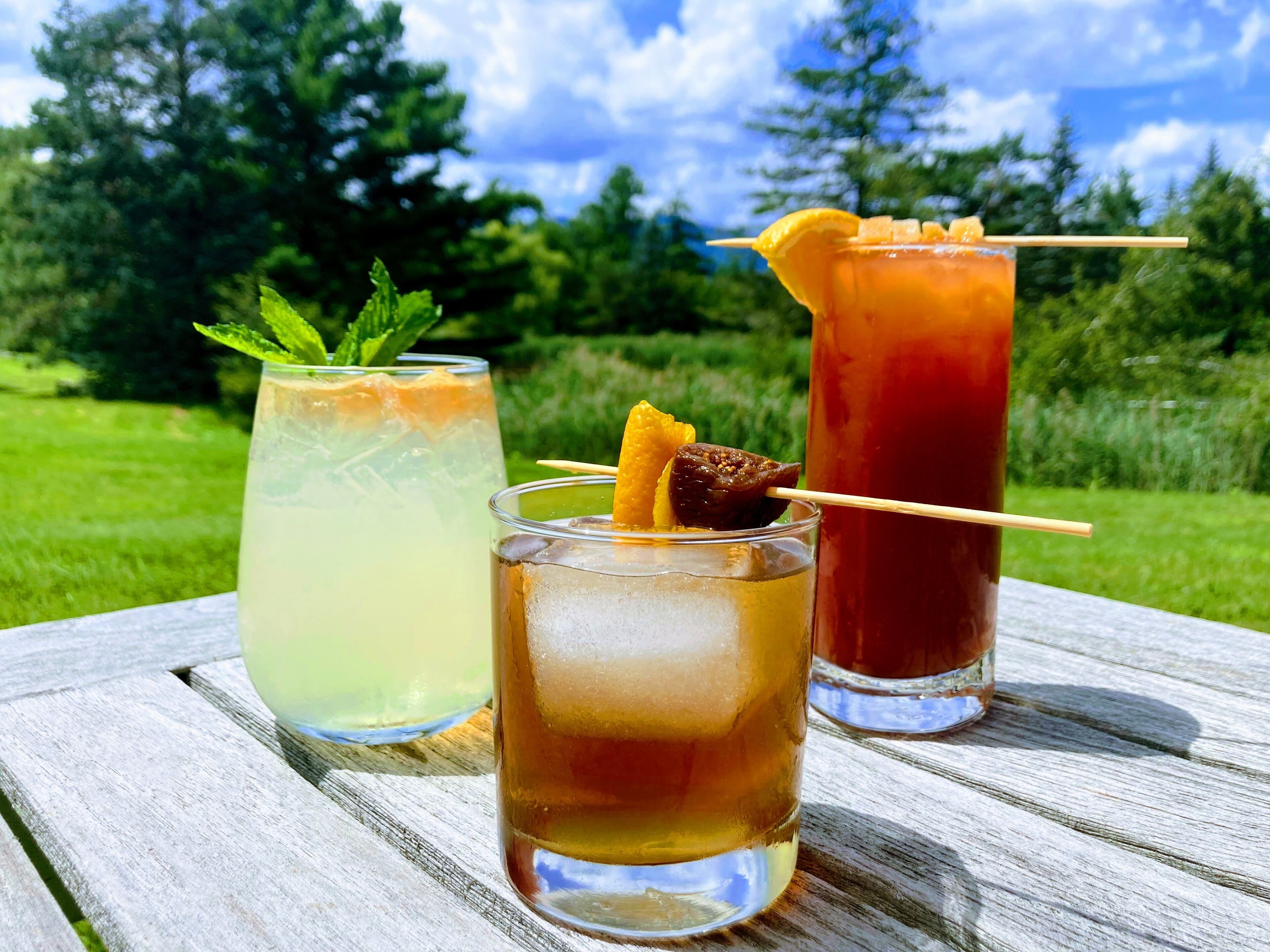 Três bebidas sobre uma mesa de madeira com fundo gramado.