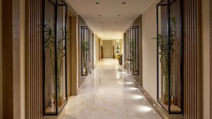 Um corredor com piso de mármore polido, ladeado por painéis verticais de madeira e vitrines de vidro com plantas.