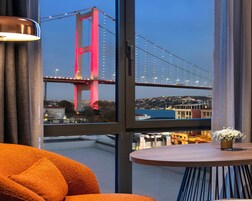 Quarto com uma grande janela com vista para uma ponte, uma mesa com um vaso de flores e um sofá.