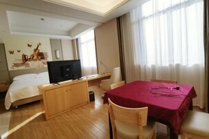 Quarto de hotel com cama, escrivaninha com computador, mesa com toalha vermelha e janela com cortinas.