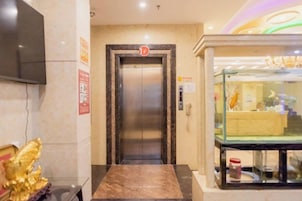 Um elevador com visor digital, uma receção com estátua dourada e uma vitrine de vidro com objetos.
