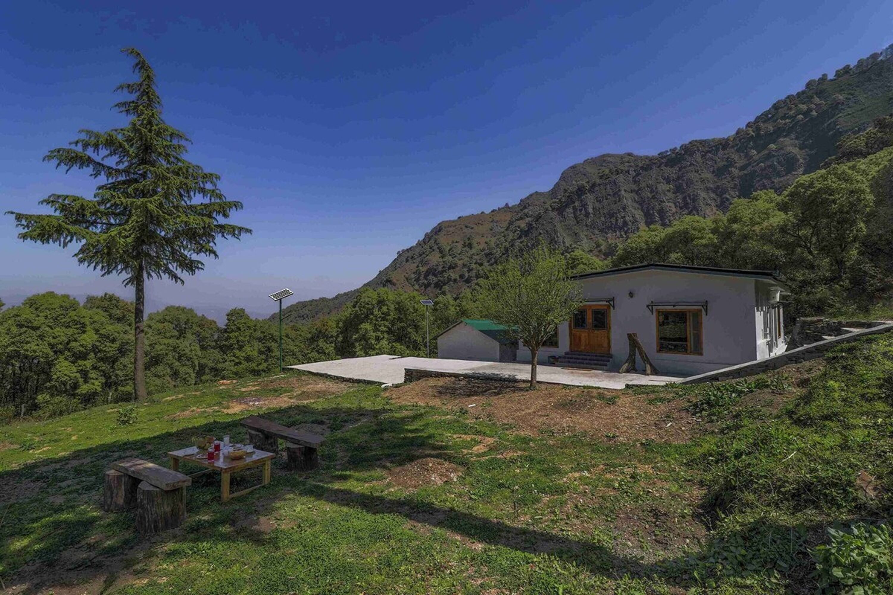 Uma casa moderna com um espaço de varanda, rodeada por vegetação exuberante e com uma montanha ao fundo.