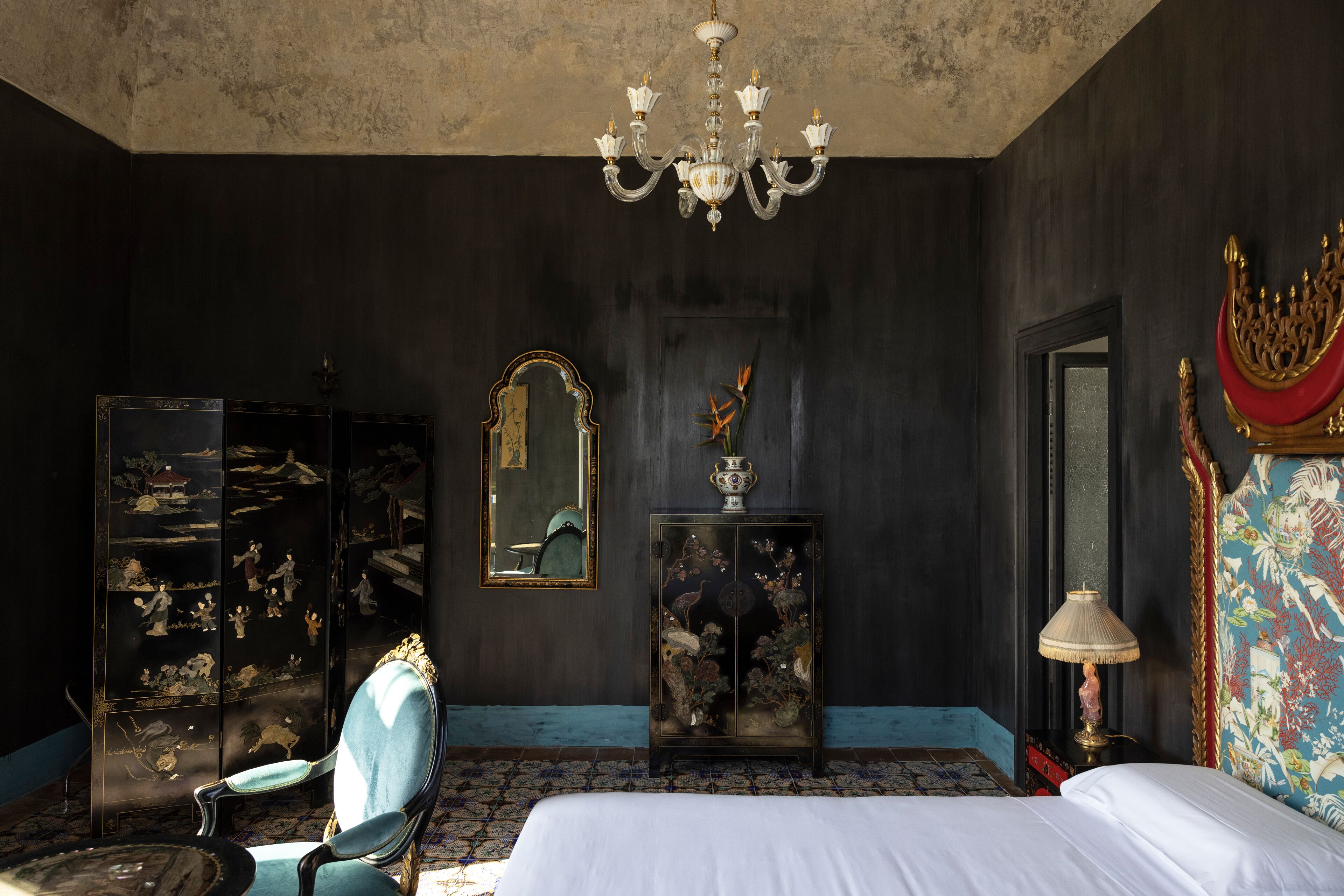 Quarto com cama, uma cadeira, cômoda, espelho e lustre.