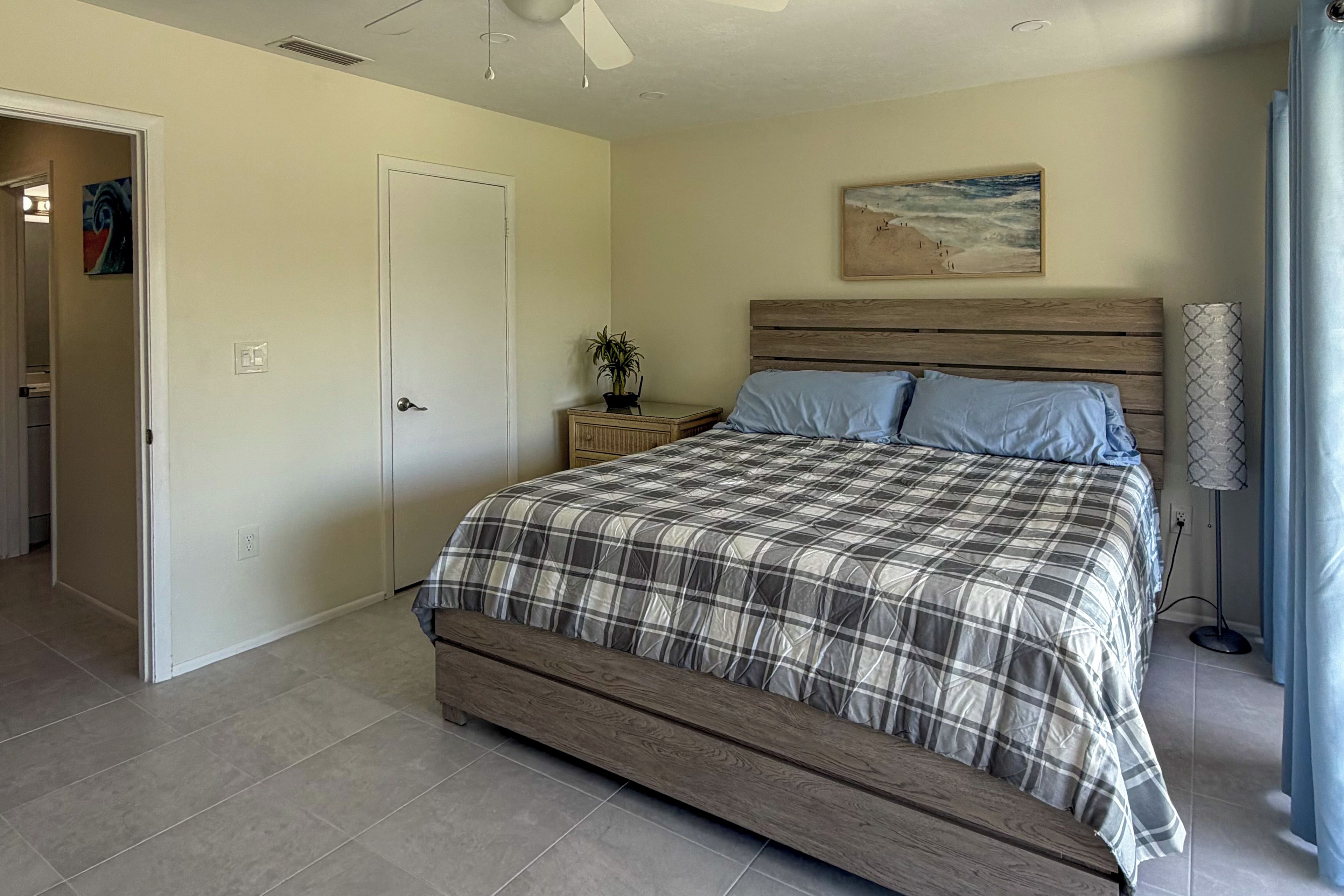 Quarto com cama, mesa de cabeceira, planta em vaso, quadro na parede e ventilador de teto.