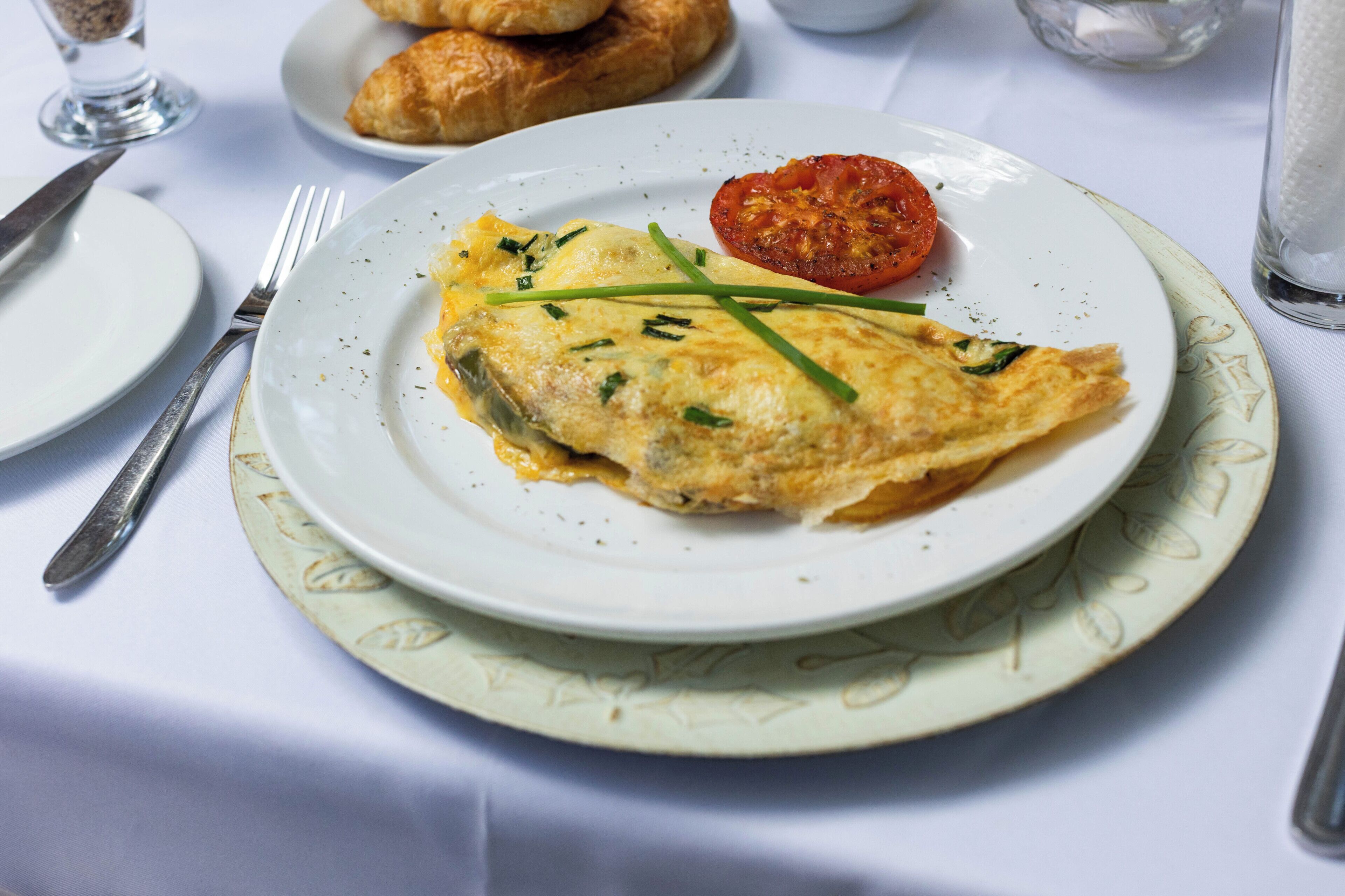 Um prato com omelete, uma fatia de tomate e cebolinha verde sobre um prato branco com borda verde.
