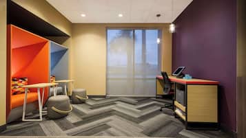 Um espaço de escritório moderno com carpete em padrão herringbone, uma mesa com computador e uma área de estar colorida com pufes.