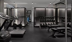 Uma academia com equipamentos de cardio, halteres e suportes para pesos.