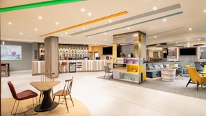 Um saguão moderno de hotel com área de bar, assentos e uma tela de televisão.