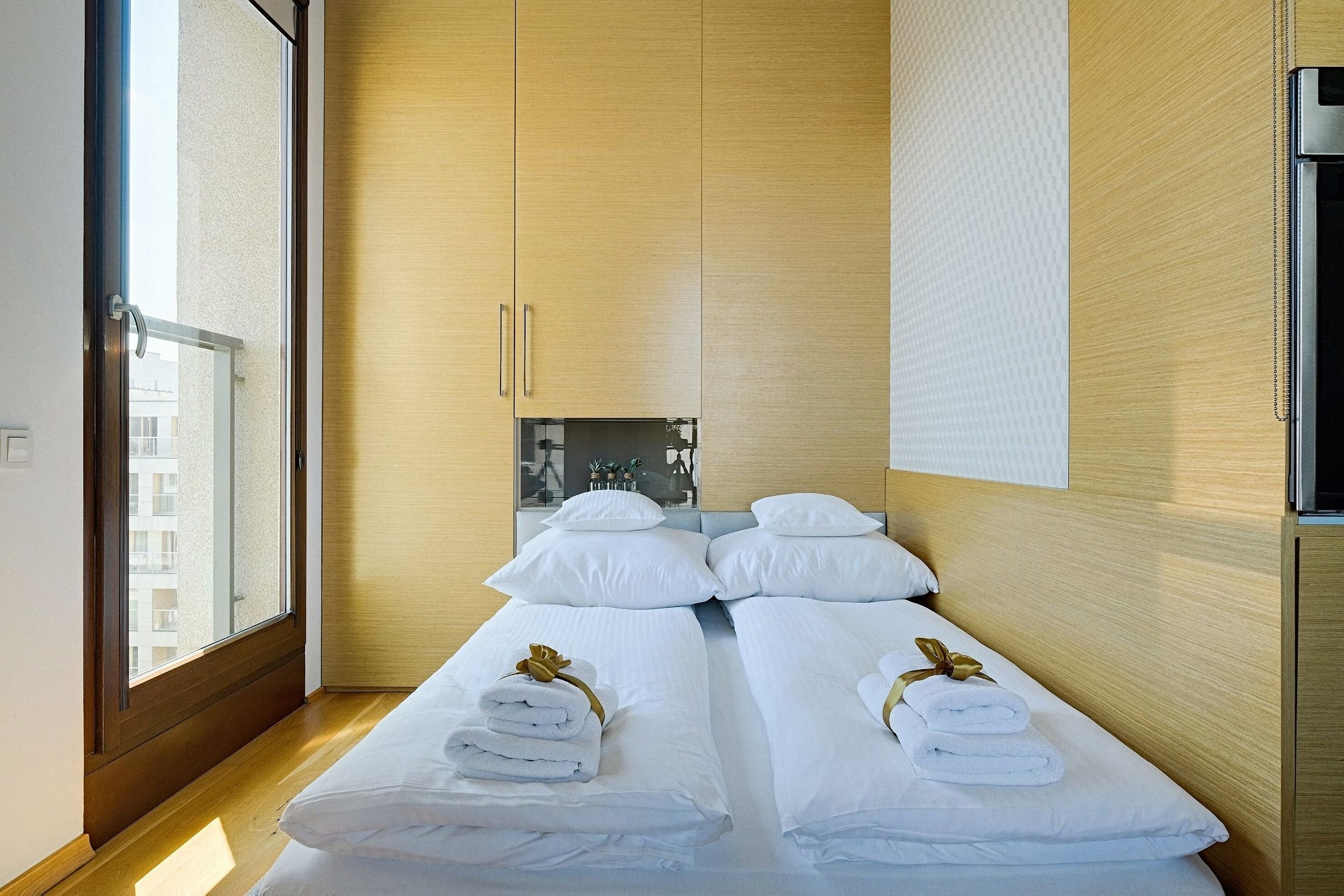 Quarto de hotel com cama, guarda-roupa de madeira e janela com vista para edifícios.