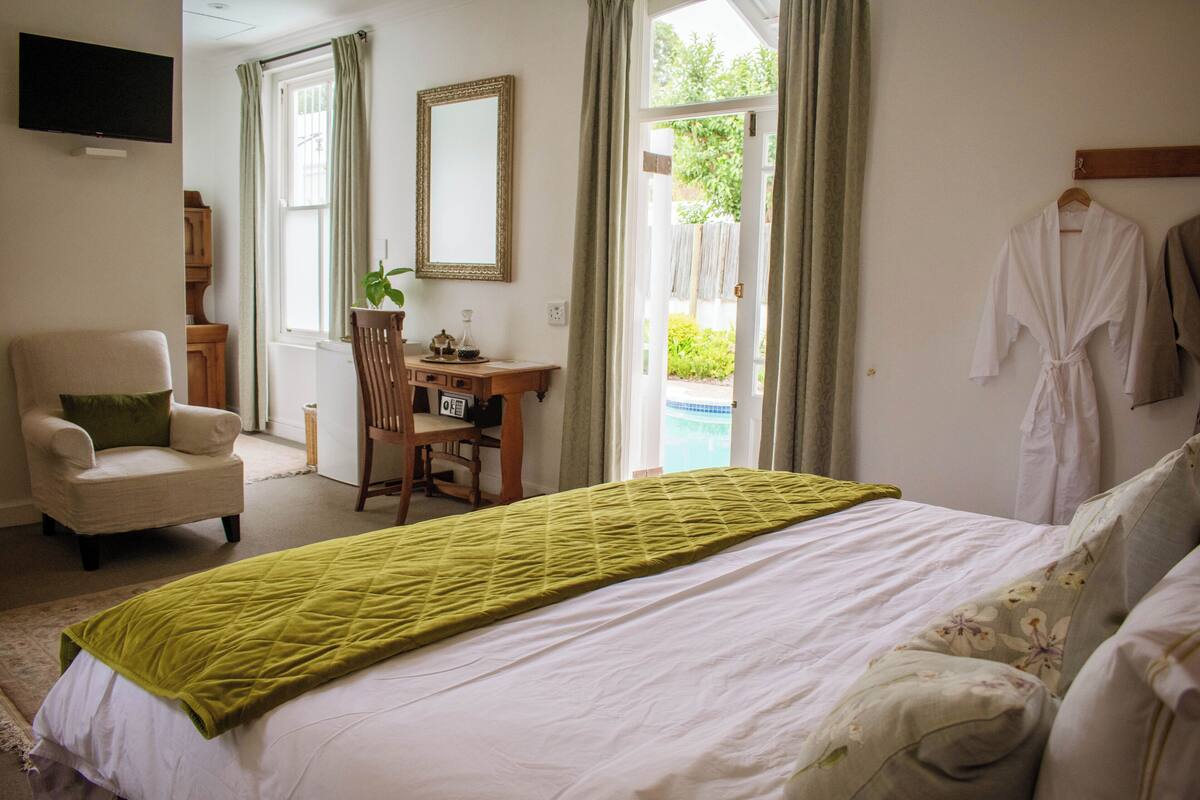 Um quarto com cama, escrivaninha, cadeira, televisão e roupão pendurado na parede.