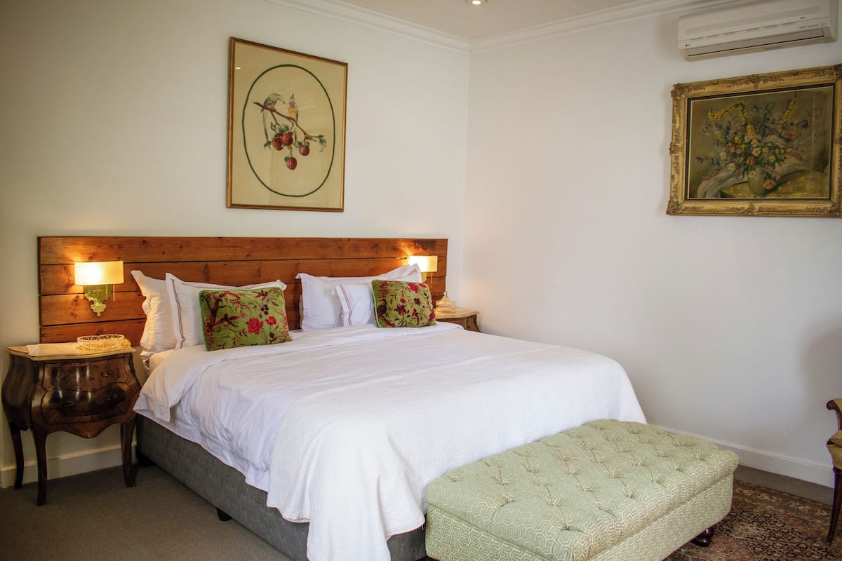 Cama bem arrumada com lençóis brancos, cabeceira de madeira e duas luminárias de cabeceira.