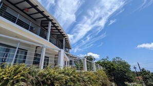 Um edifício moderno com várias varandas, janelas amplas e vegetação exuberante em primeiro plano.