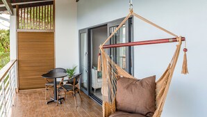 Uma cadeira balanço com almofada, uma mesa redonda pequena com cadeiras, e uma porta deslizante que dá para um espaço interno.