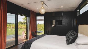Quarto com cama grande, vista para vinhedo através de porta deslizante e luminária no teto.