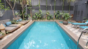 Uma piscina interior retangular com chão em azulejo, rodeada por espreguiçadeiras e plantas em vasos.