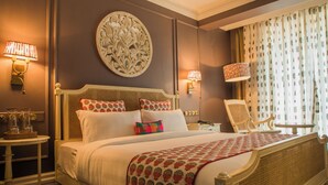 Quarto de hotel bem arrumado, com uma cama grande, duas mesas de cabeceira, uma cadeira e um objeto decorativo na parede.
