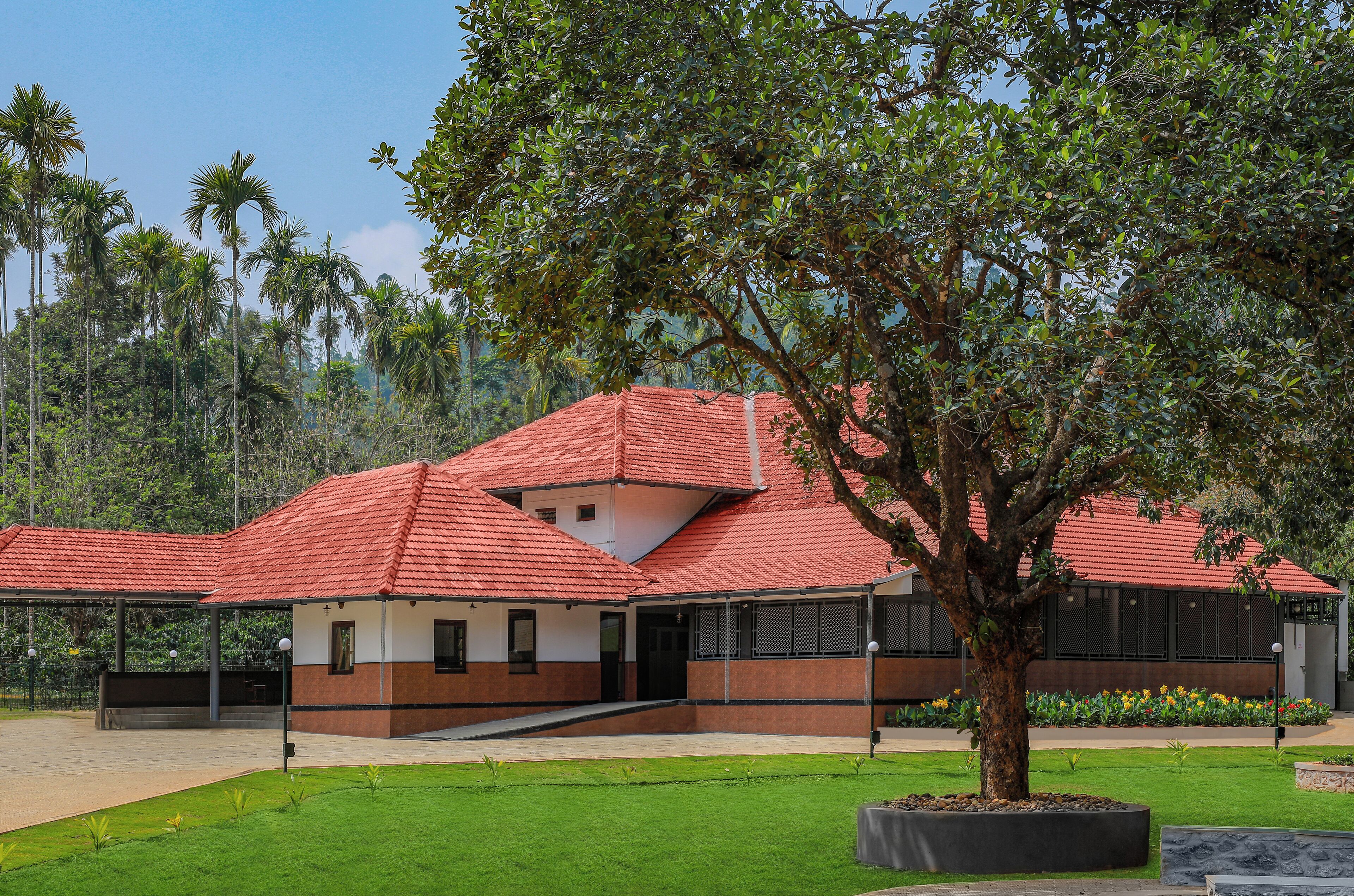 Um edifício com telhado vermelho e paredes brancas, rodeado por um jardim bem cuidado e árvores.