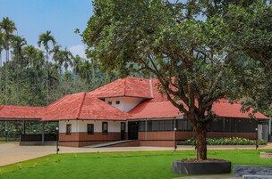 Um edifício com telhado vermelho e paredes brancas, rodeado por um jardim bem cuidado e árvores.
