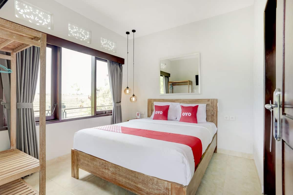 Um quarto com cama de madeira, uma janela grande com cortinas, um banco de madeira e uma luminária pendente.