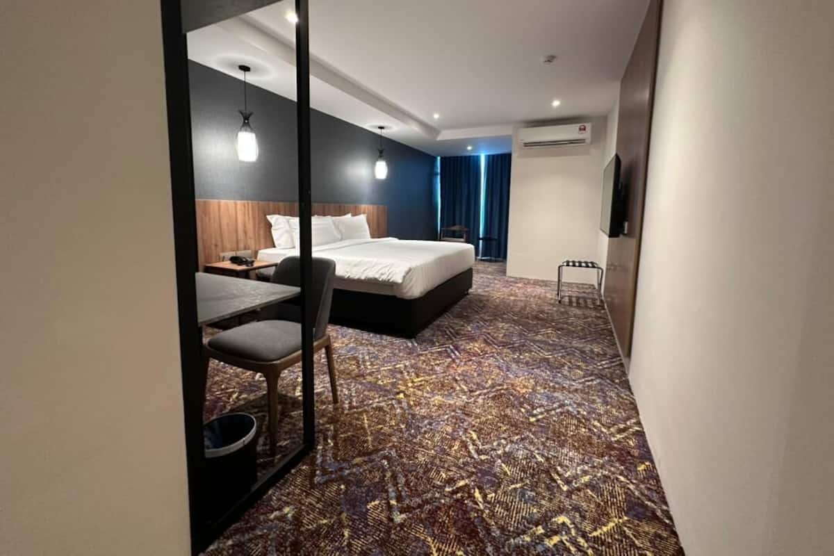 Quarto de hotel moderno com uma cama grande, uma escrivaninha com cadeira, uma mesinha e um espelho.