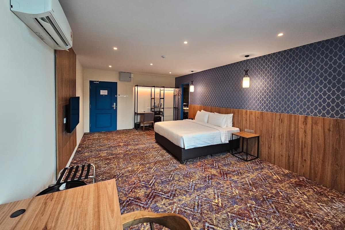 Quarto de hotel com cama, escrivaninha, cadeira, ar condicionado e porta azul.