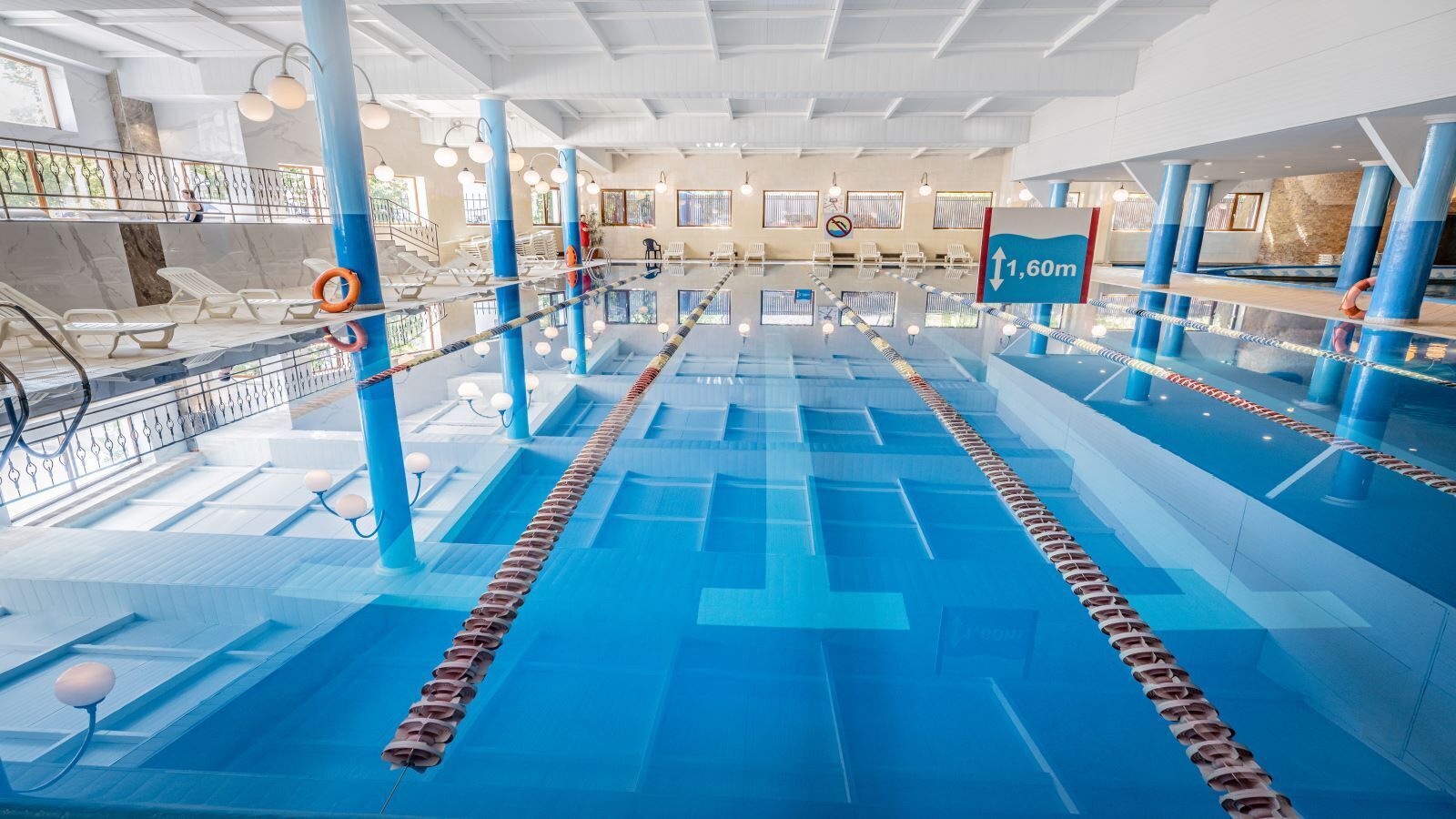 Piscina interior com faixas de separação bem definidas, cadeira de salva-vidas e placa indicando 1,60m de altura.