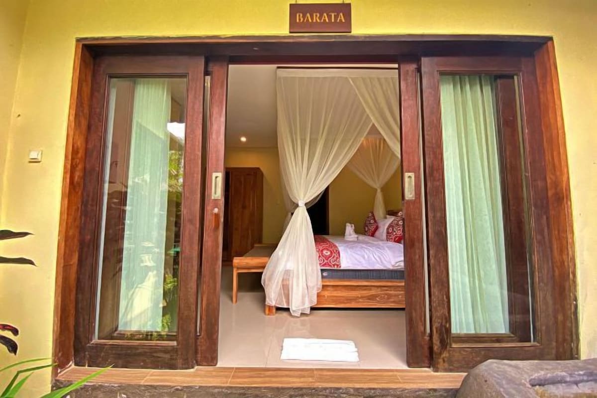 Quarto com uma cama, porta de madeira e um aviso que diz 'BARATA'.