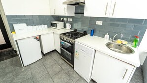 Uma cozinha compacta com armários brancos, micro-ondas, fogão a gás, lava-louças e pia.