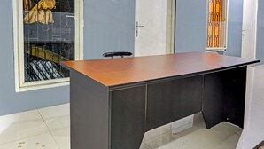 Um quarto com uma grande escrivaninha de madeira, uma cadeira, uma janela com grades de metal e uma porta.
