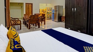 Quarto de hotel com cama, cadeiras de madeira, mesa de jantar, frigorífico e guarda-roupa.